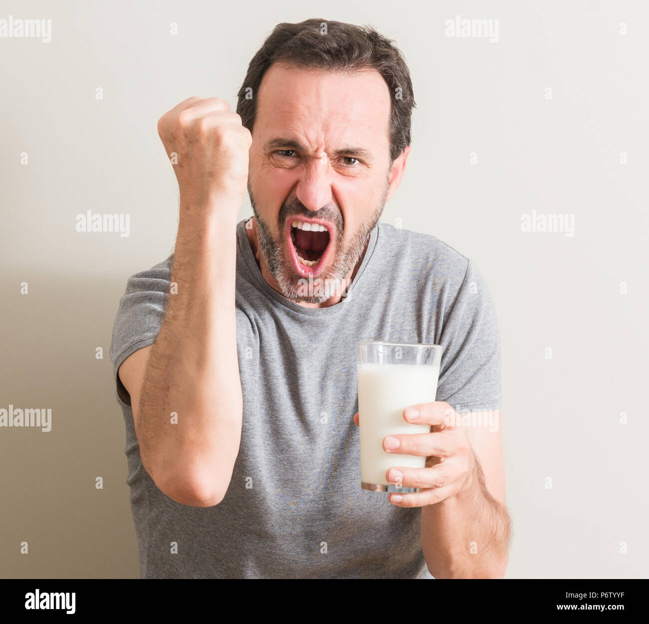 Senior man drinking a glass of milk annoyed and frustrated shouting ...