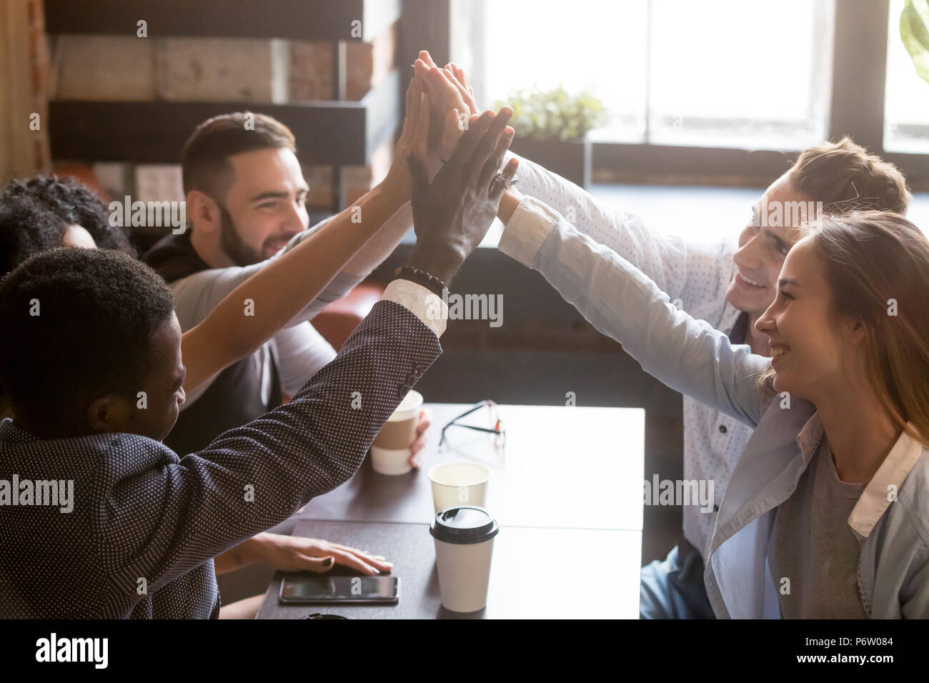 Multiracial friends giving high five sitting out in coffee shop Stock ...