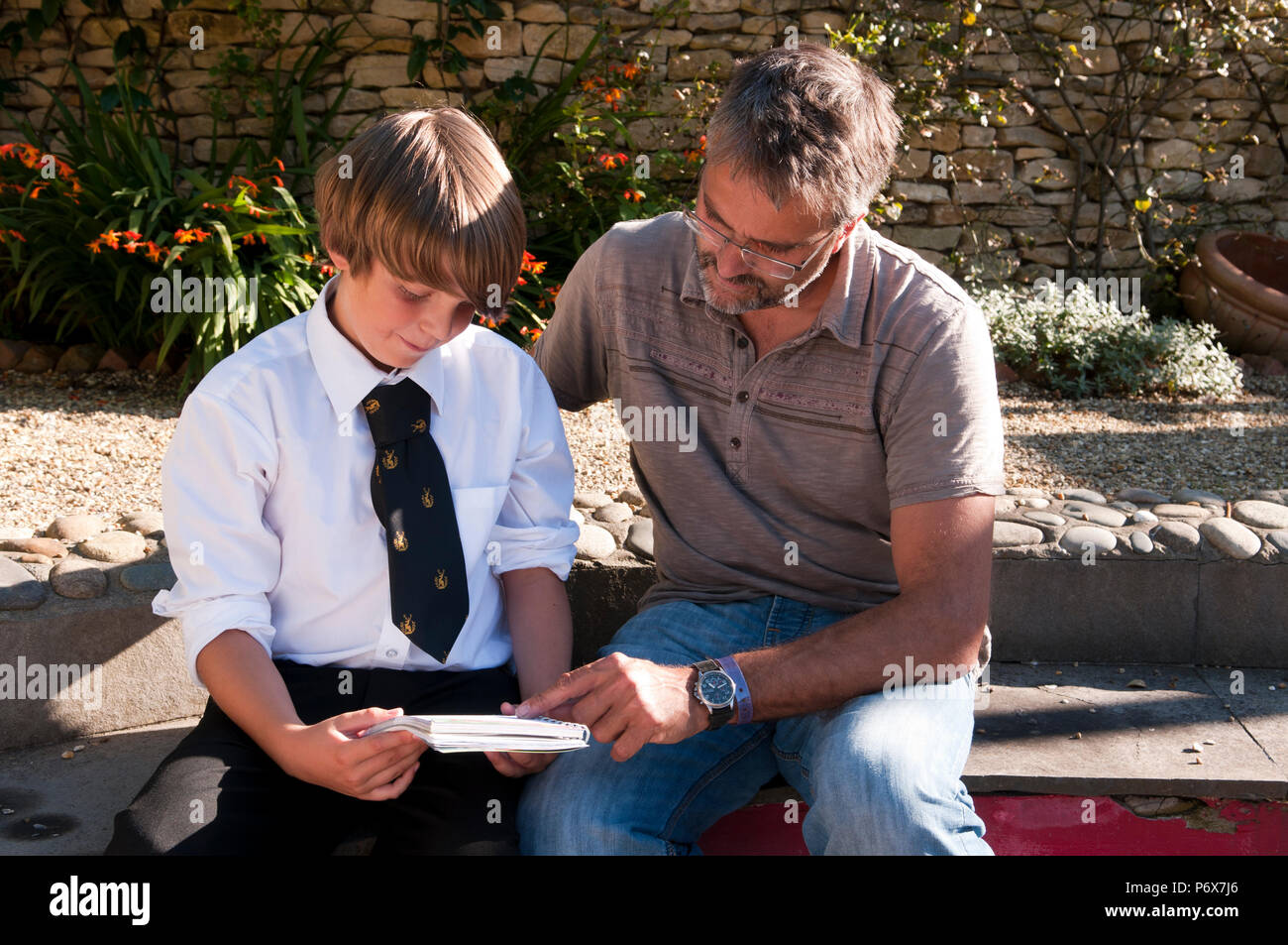 Schoolboy sitting in garden showing his father his schoolwork Stock ...