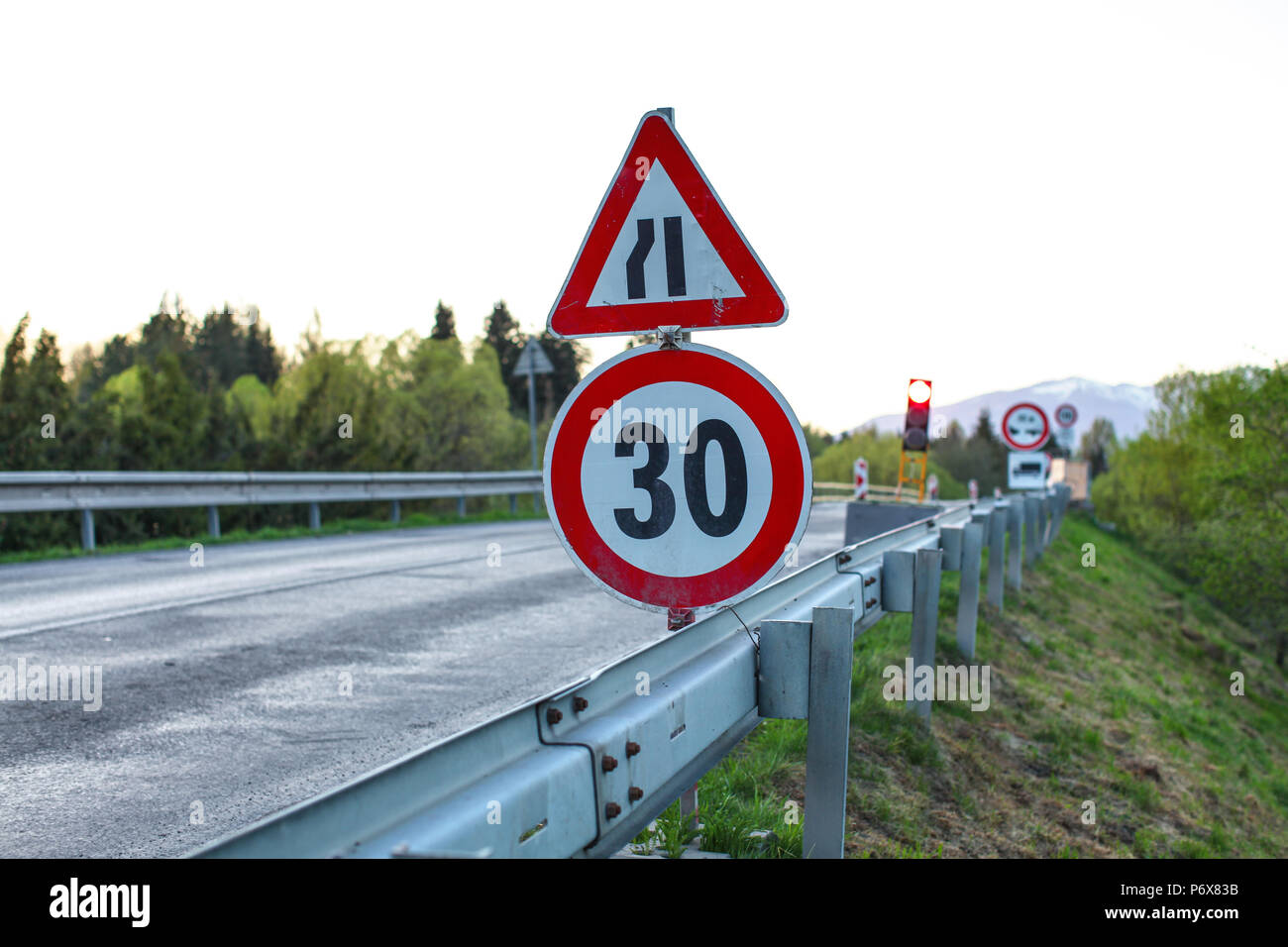 Road sign, reduce speed to 30, blurred red traffic light and ...