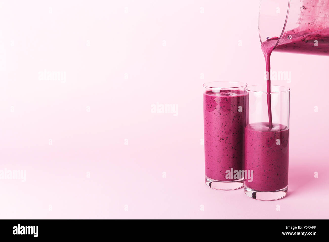 Two glasses of blueberries smoothie on pink background. Poring from ...