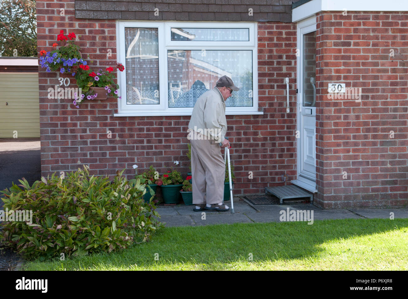 Side view of elderly man with walking sticks walking towards his home ...