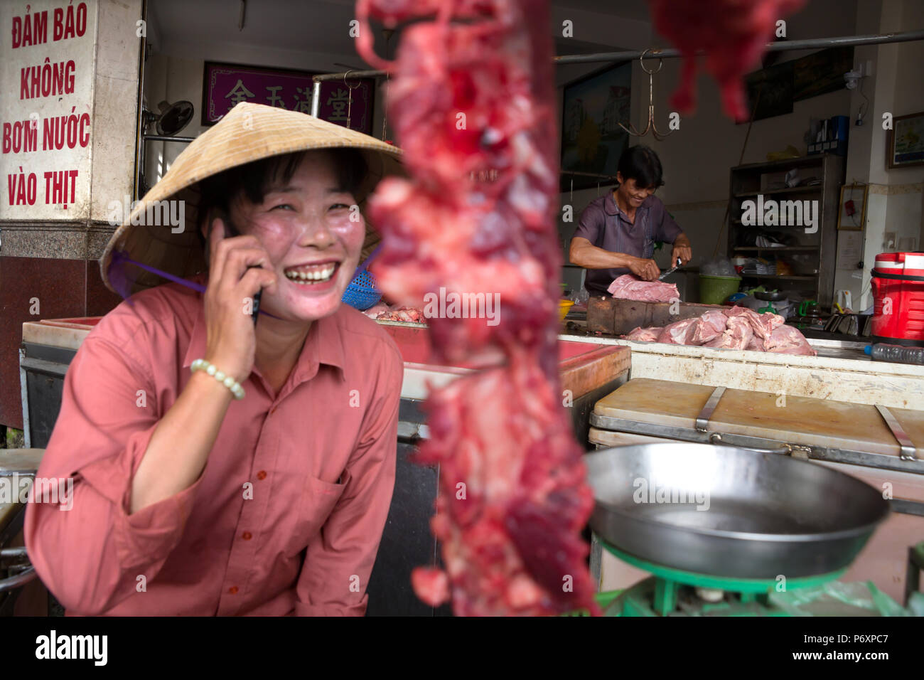 Woman butcher selling meat and on the phone with conical hat in Can Tho ...