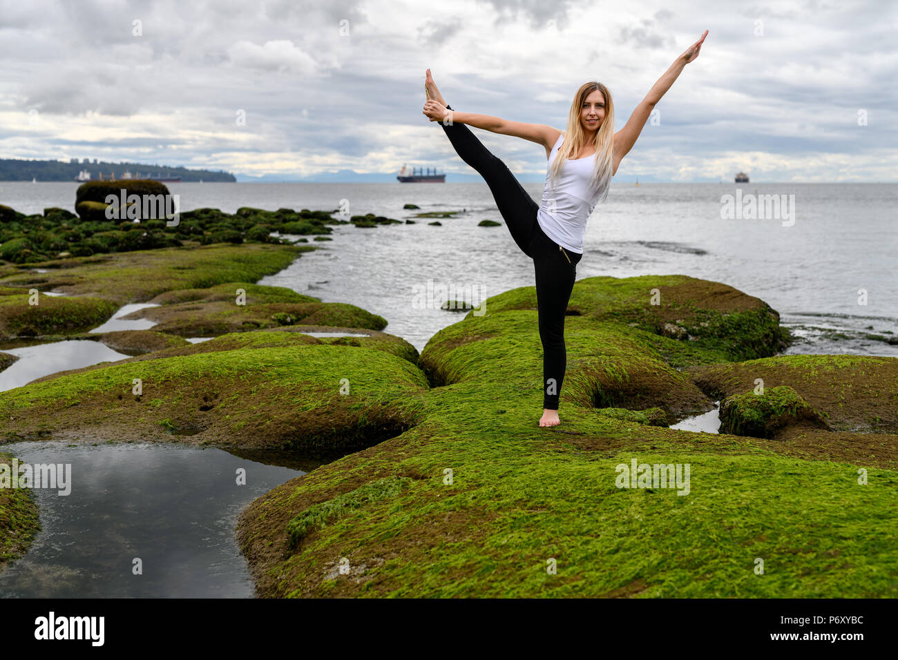 Young woman doing acrobatic exercises at the intertidal zone of Stanley ...
