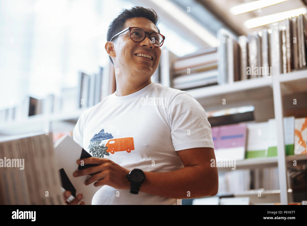 Young happy man reading and looking aside in a bright modern book store ...