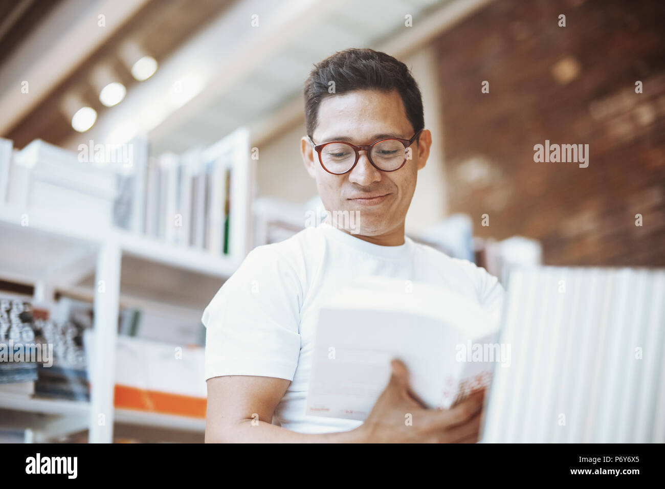 Young attractive man in white t-shirt smiling and reading book with ...