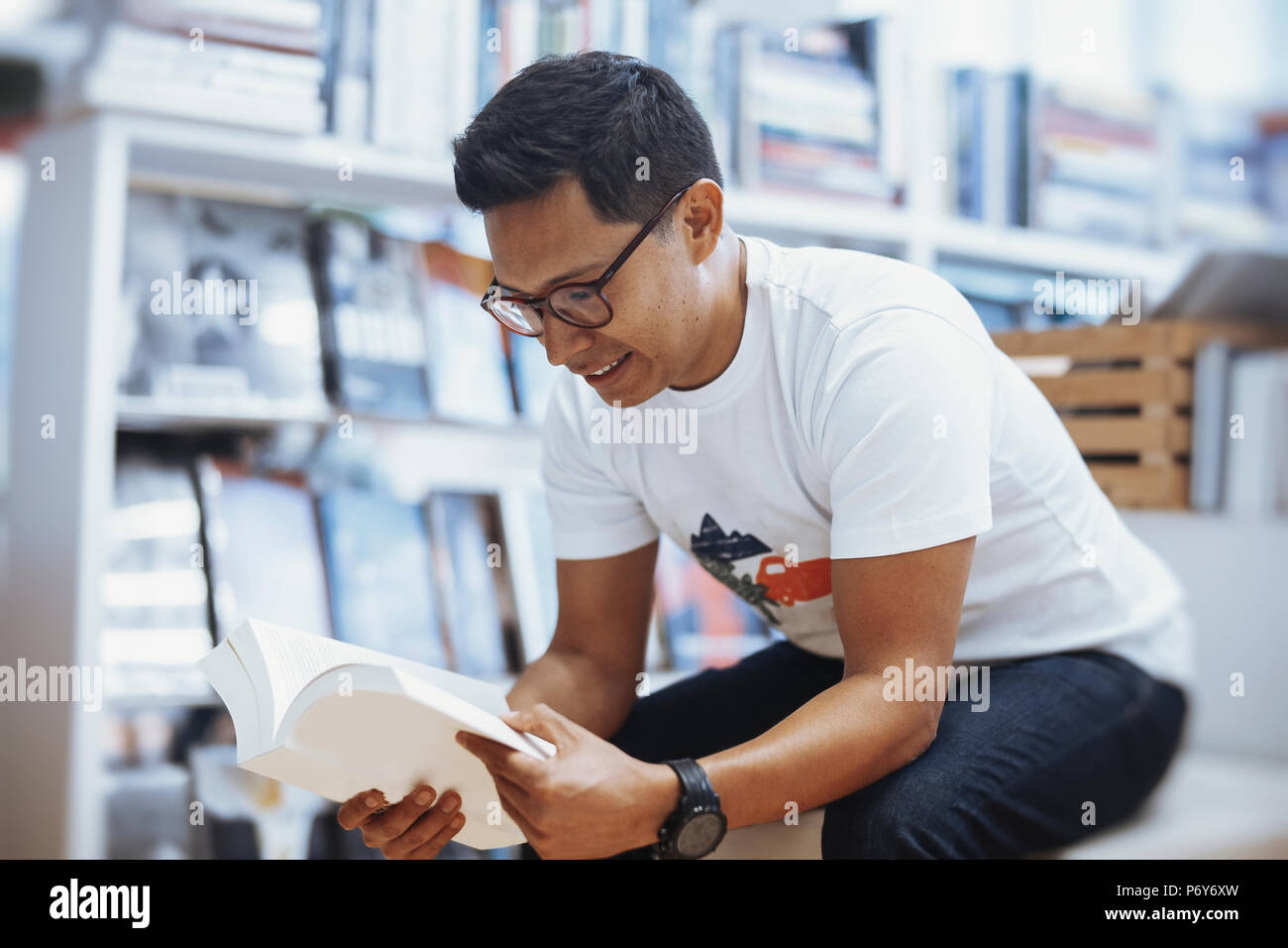 Young spectacled brunette man sitting and reading book with blank cover ...