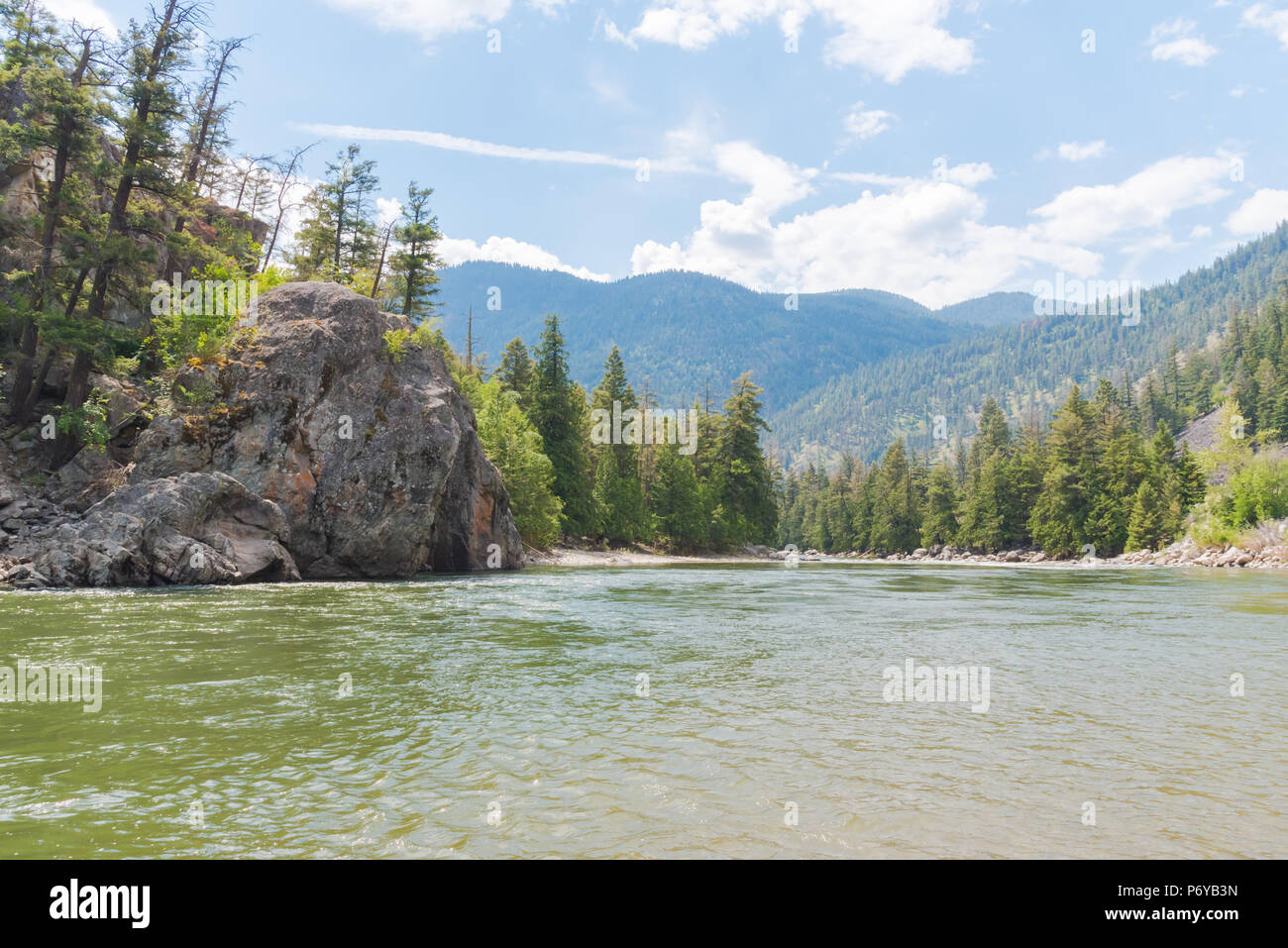 River with rock bluffs and pine forest with mountains and blue sky in ...