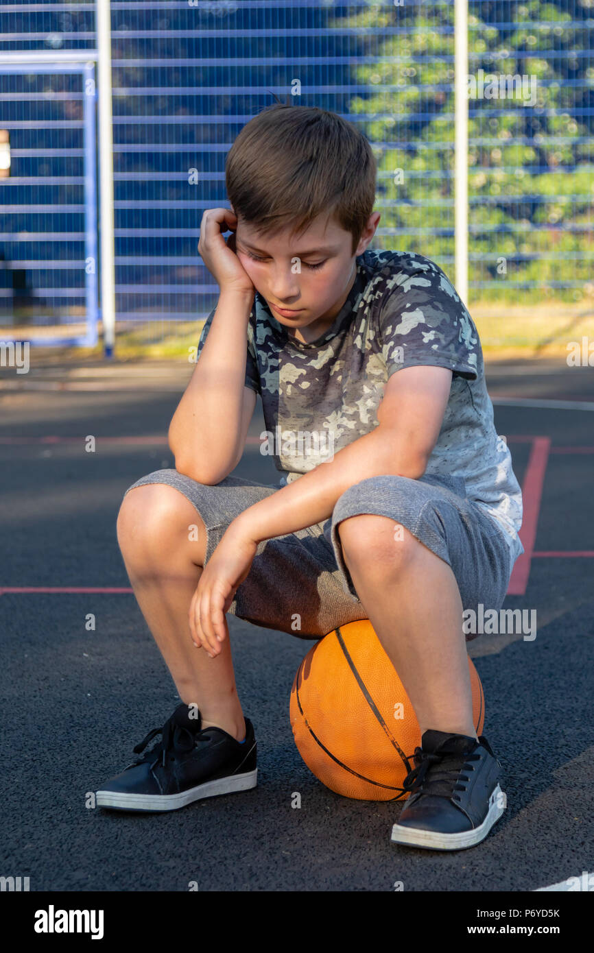 Unhappy boy sitting on a basketball. Losing game or not picked for a ...