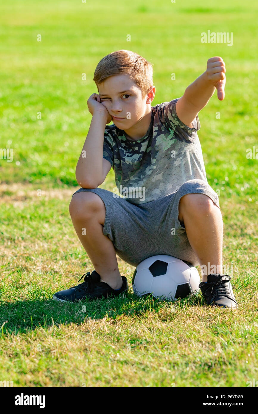 Sad looking pre-teen boy sitting on a ball. Lost game or not picked for ...