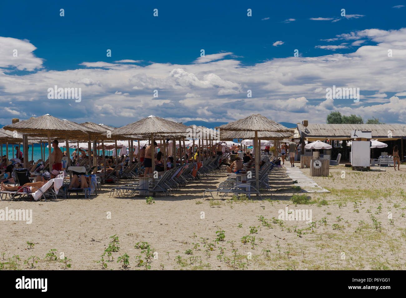 Greek Mediterranean beach bar with crowd. Bathers with sun umbrellas at ...