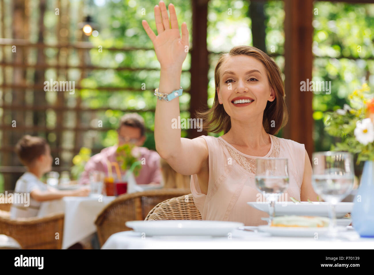Smiling dark-eyed woman lifting her hand calling waitress Stock Photo ...