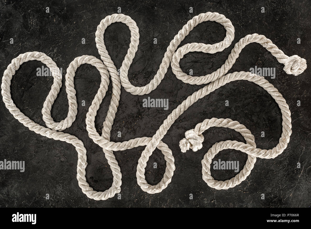 top view of white nautical rope with knots on dark concrete tabletop ...