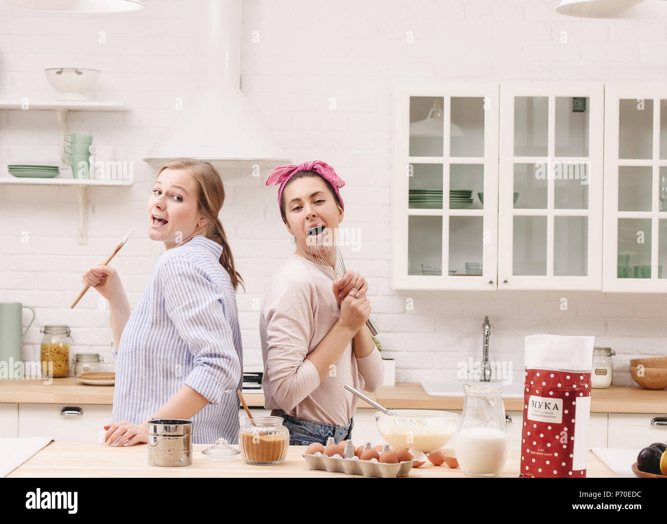 Two cheerful friends cook together desserts and sing Stock Photo - Alamy