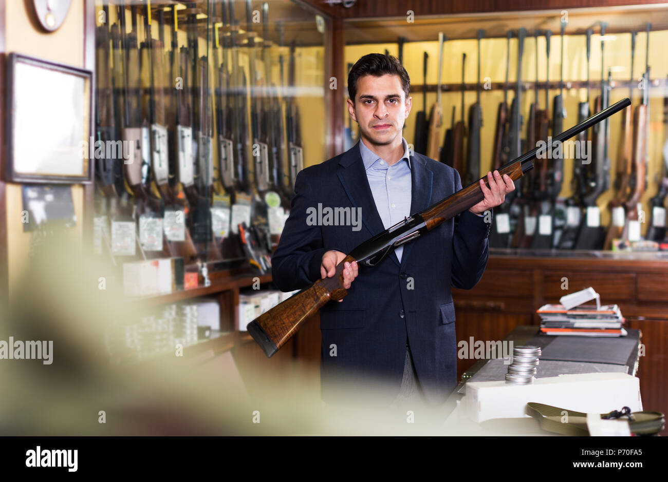 Portrait of positive salesman in gun store holding shotgun Stock Photo ...