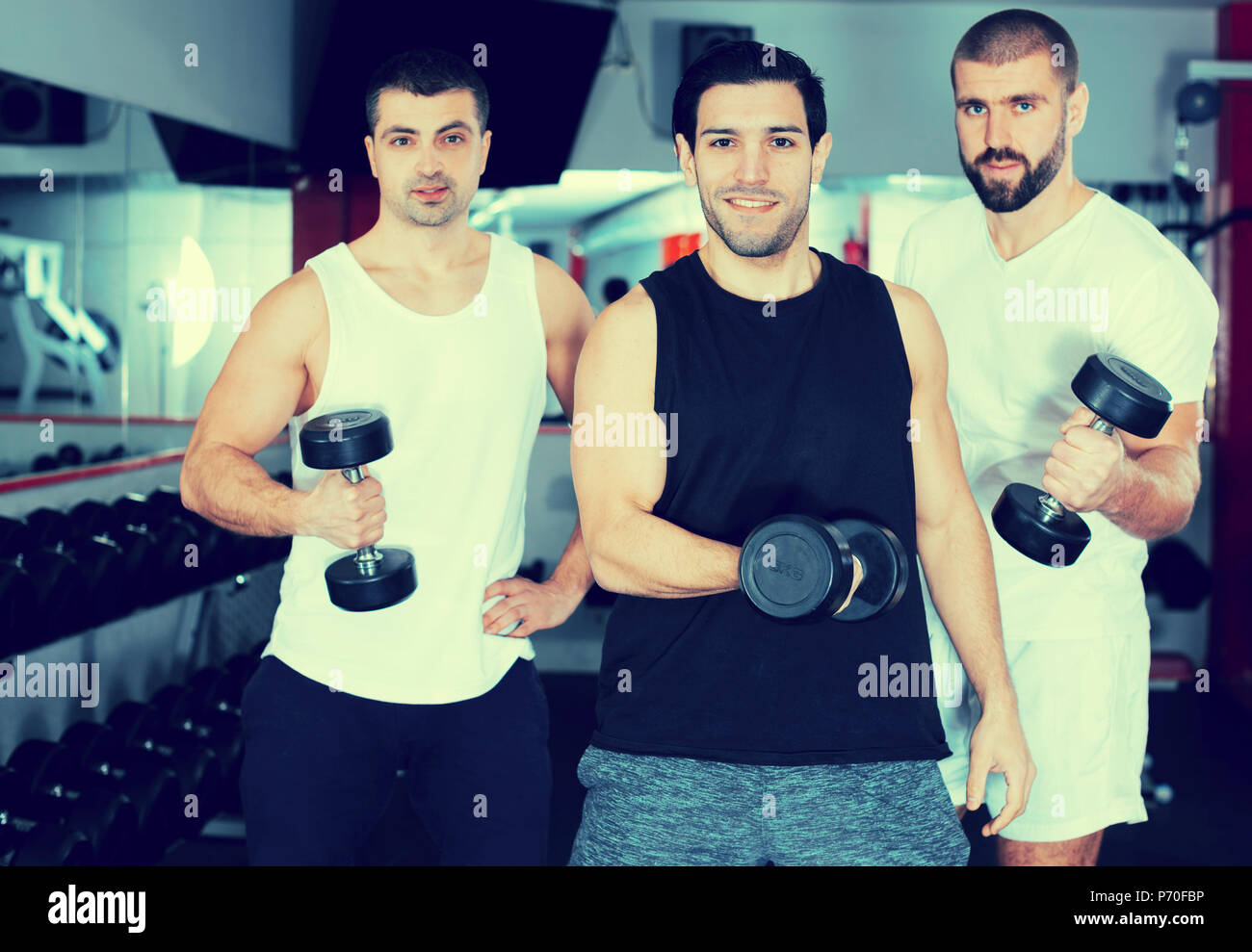 Three muscular men taking break during workout in gym, posing together ...