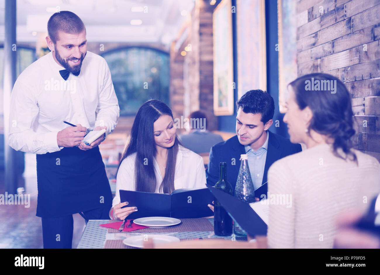 Employee smiling adult waiter man taking order from positive guests at ...