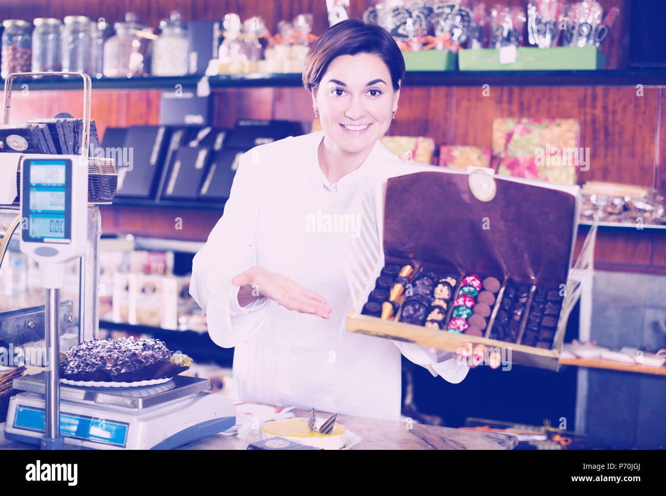 Smiling young female shop assistant demonstrating box of delicious ...