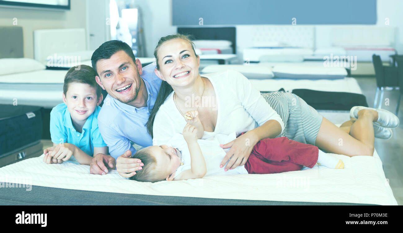 Smiling ukrainian parents with two young sons testing mattress in store ...