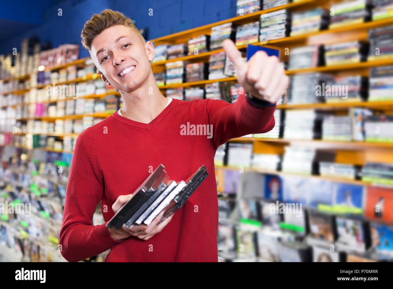 Smiling guy holding stack of DVDs bought in store giving thumbs up ...