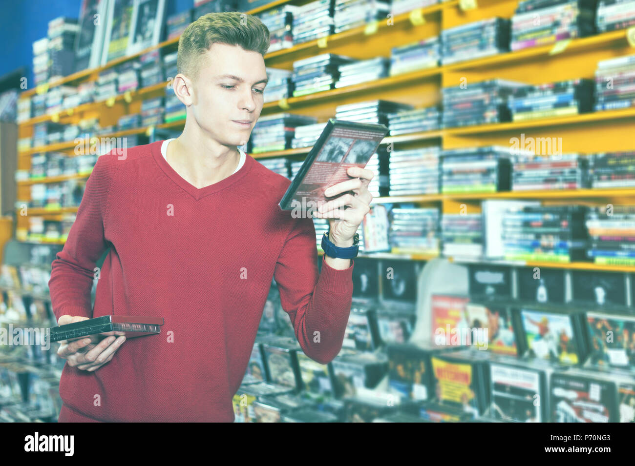 positive focused adult guy looking on box of DVD movie during shopping ...
