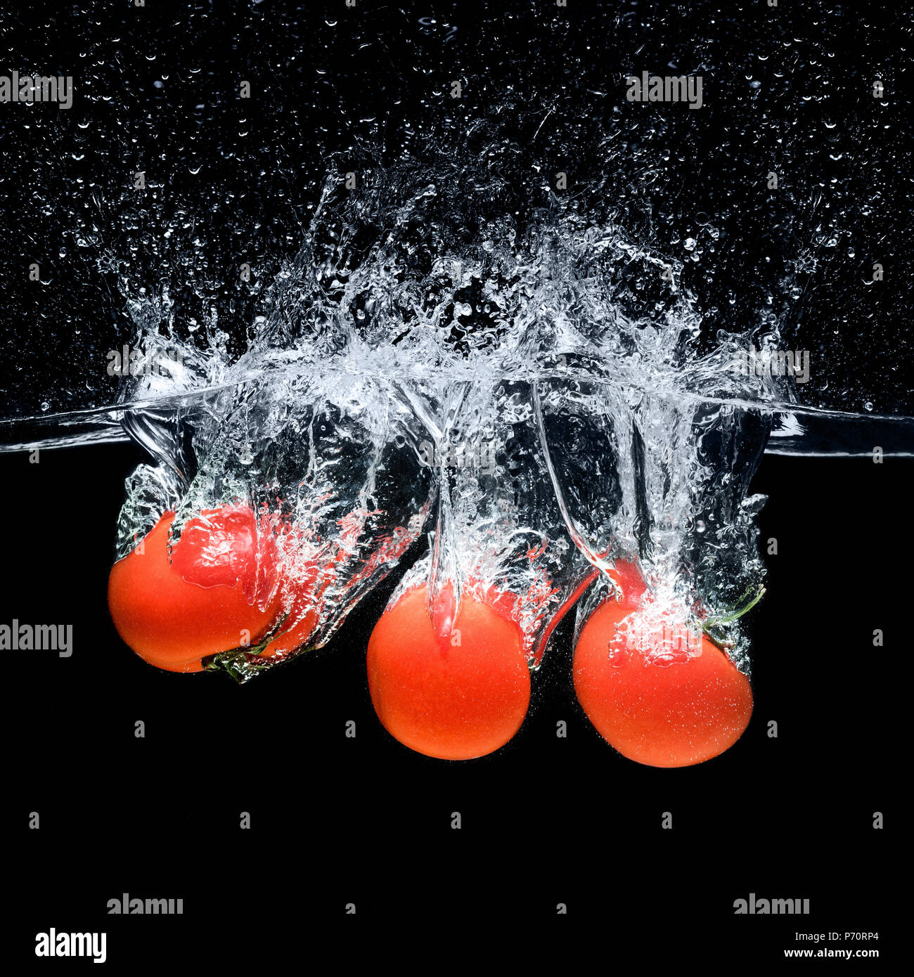 close up view of ripe tomatoes falling into water isolated on black ...