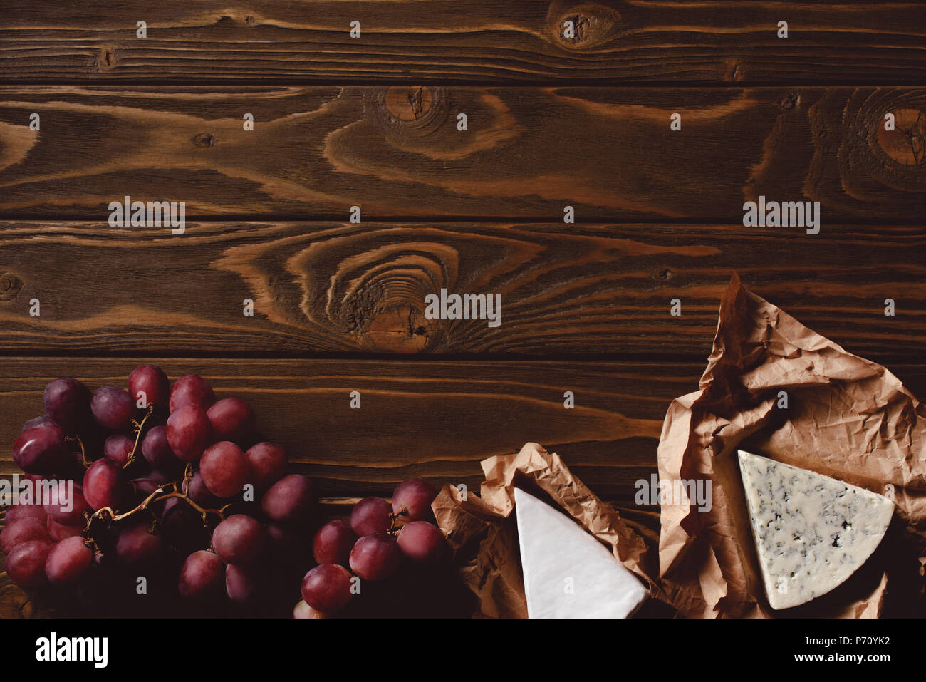 top view of slices of cheese on crumpled paper and ripe red grapes on ...