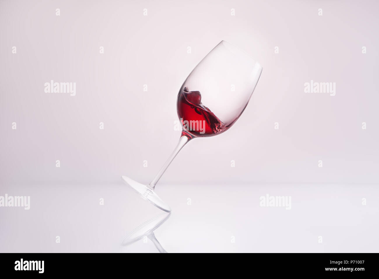 inclined glass with red wine on reflective surface and on white Stock ...