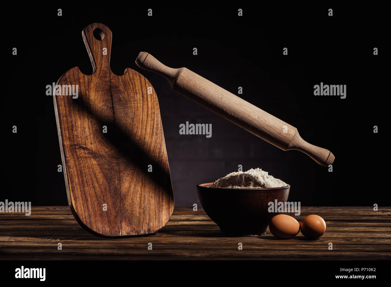 flying rolling pin, wooden cutting board, two eggs and bowl with flour ...