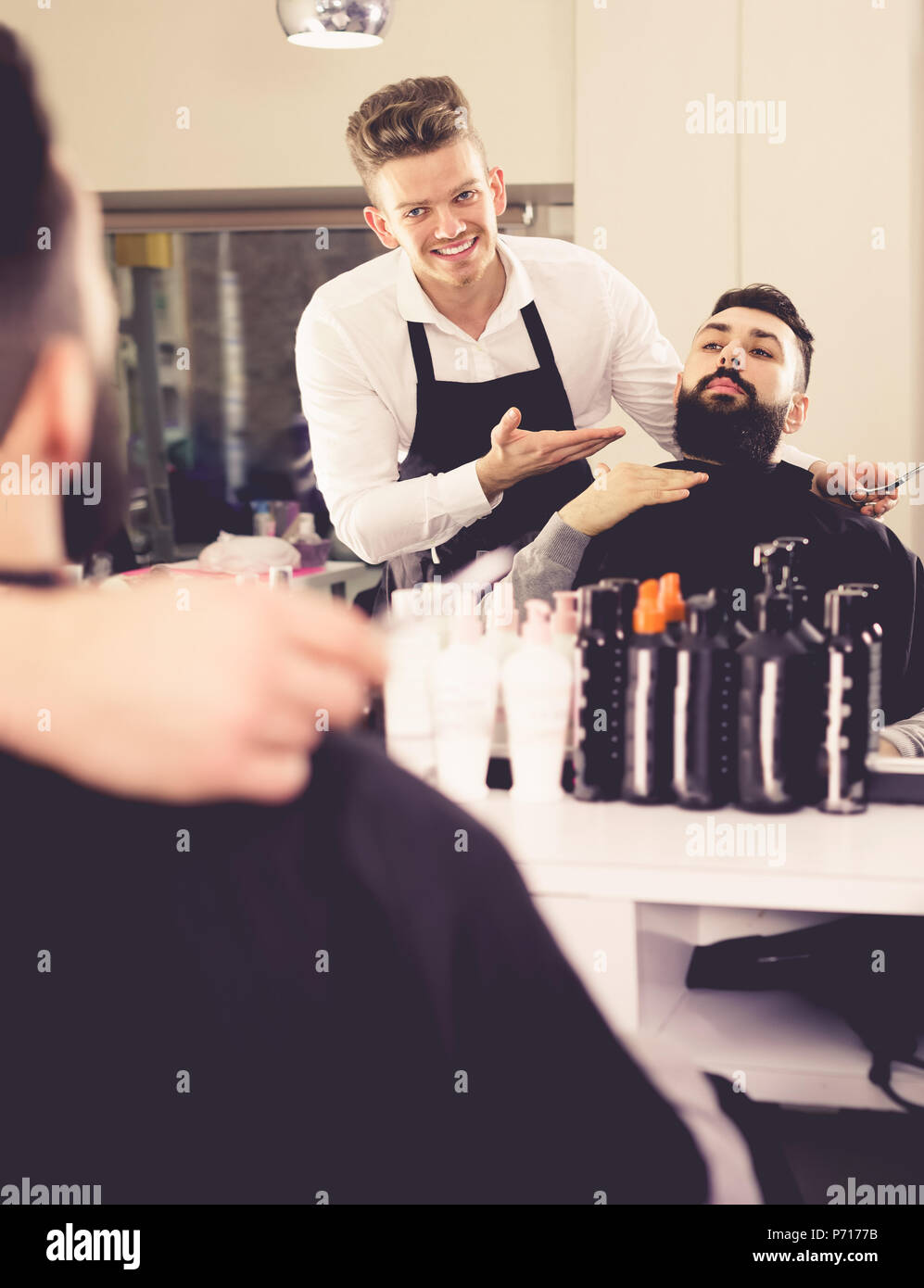 Happy man hairdresser forming beard of client into new shape at hair ...