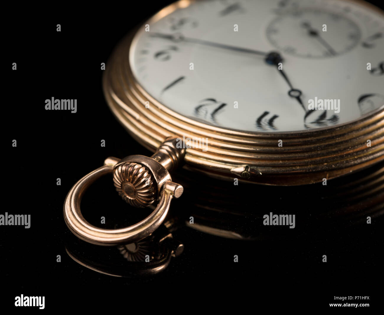 Detail of an old, used golden pocket watch on a black reflective ...