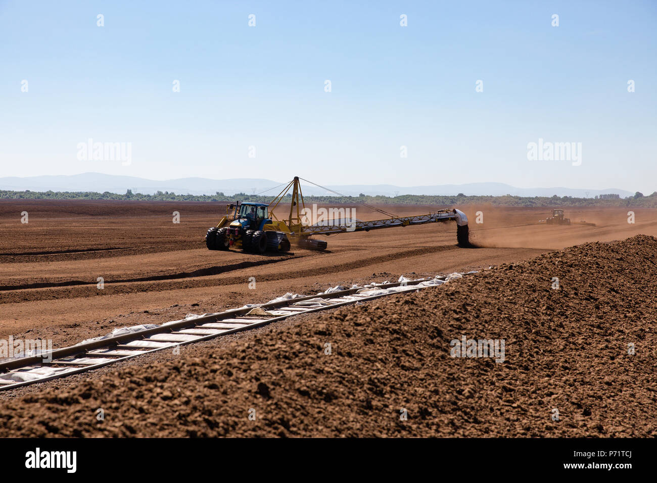 Agricultural tractor with harvester stockpiling loose milled peat ...