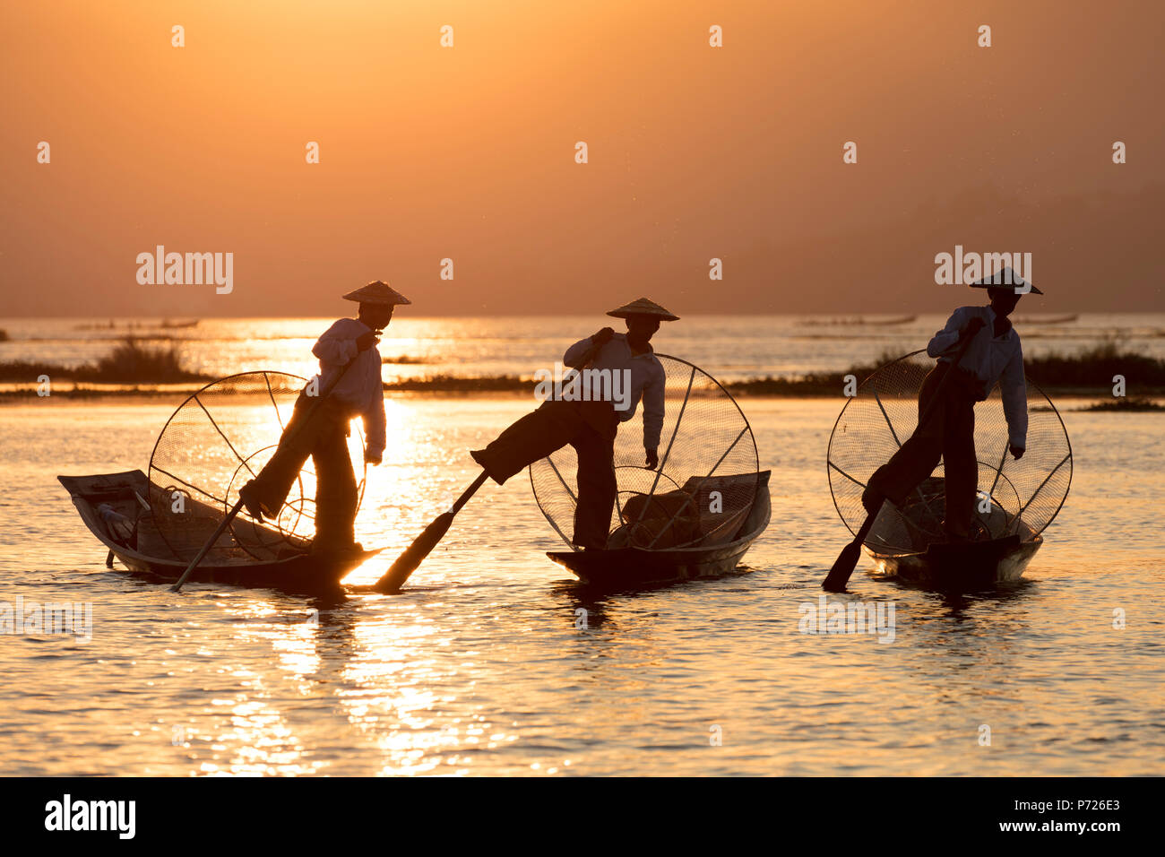 Three fishermen row with one leg at sunset on Inle Lake, Shan State ...