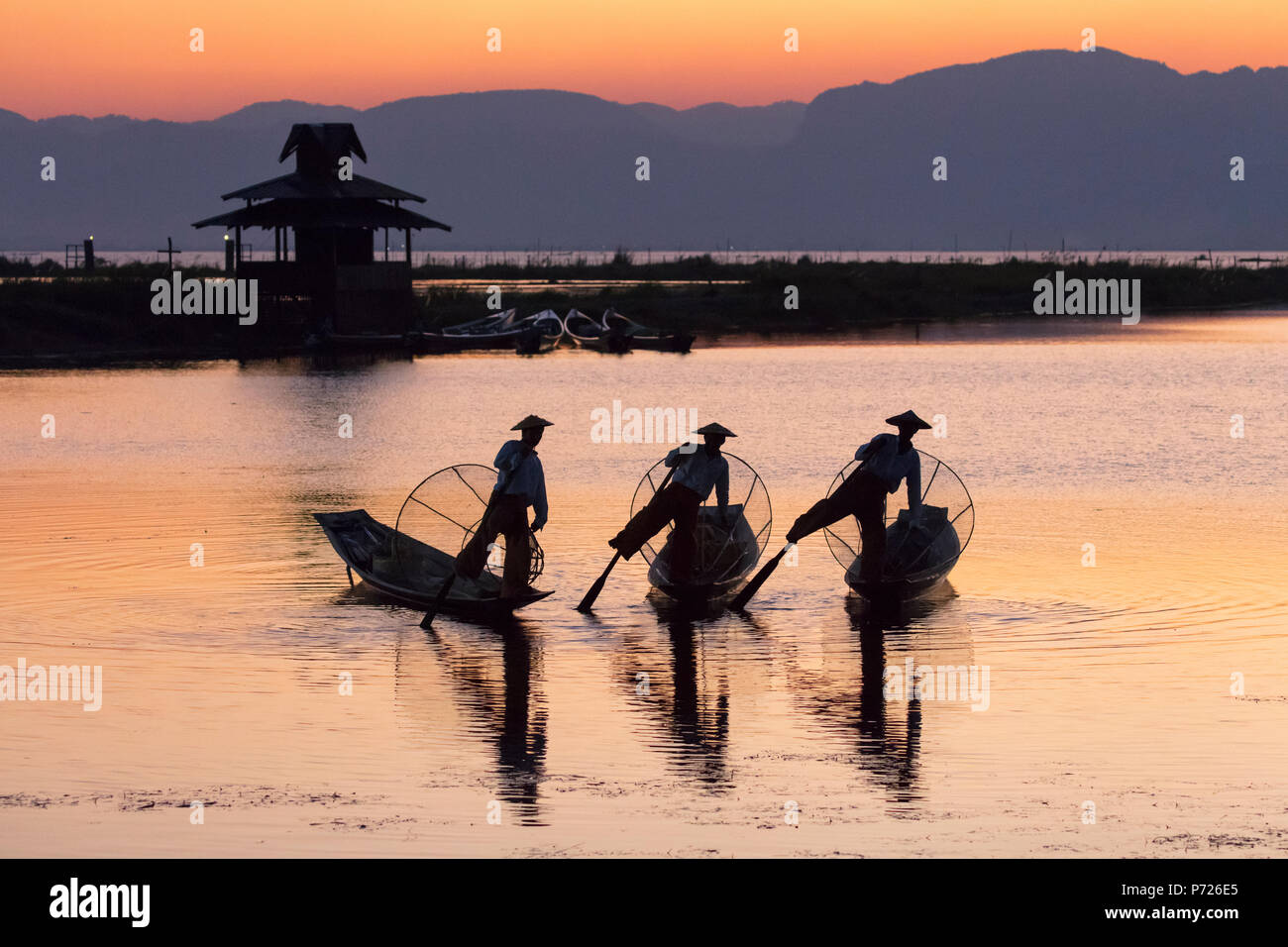 Three fishermen balance on one leg at sunset on Inle Lake, Shan State ...