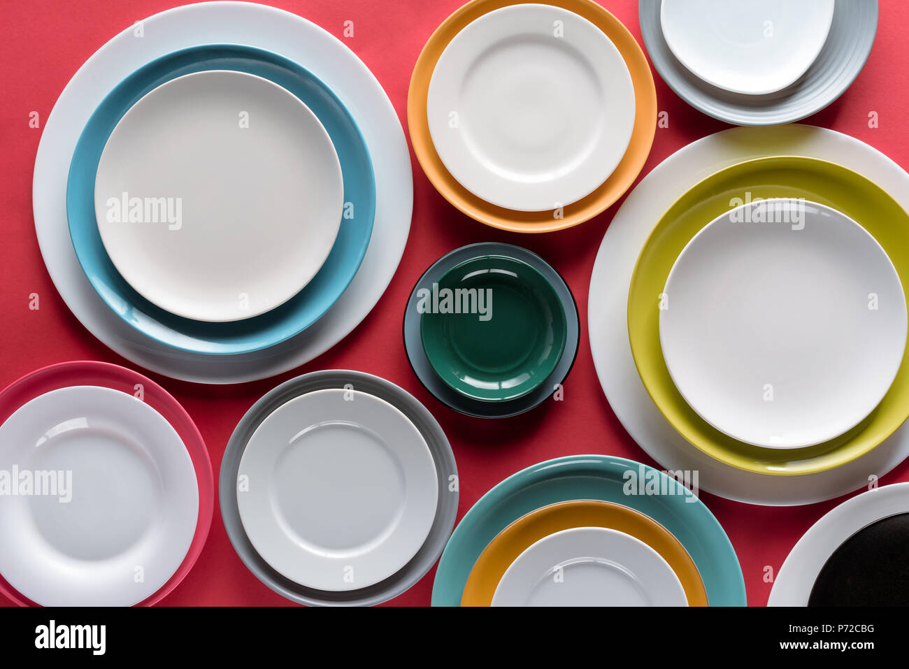 White and colorful plates of different sizes on red background Stock ...