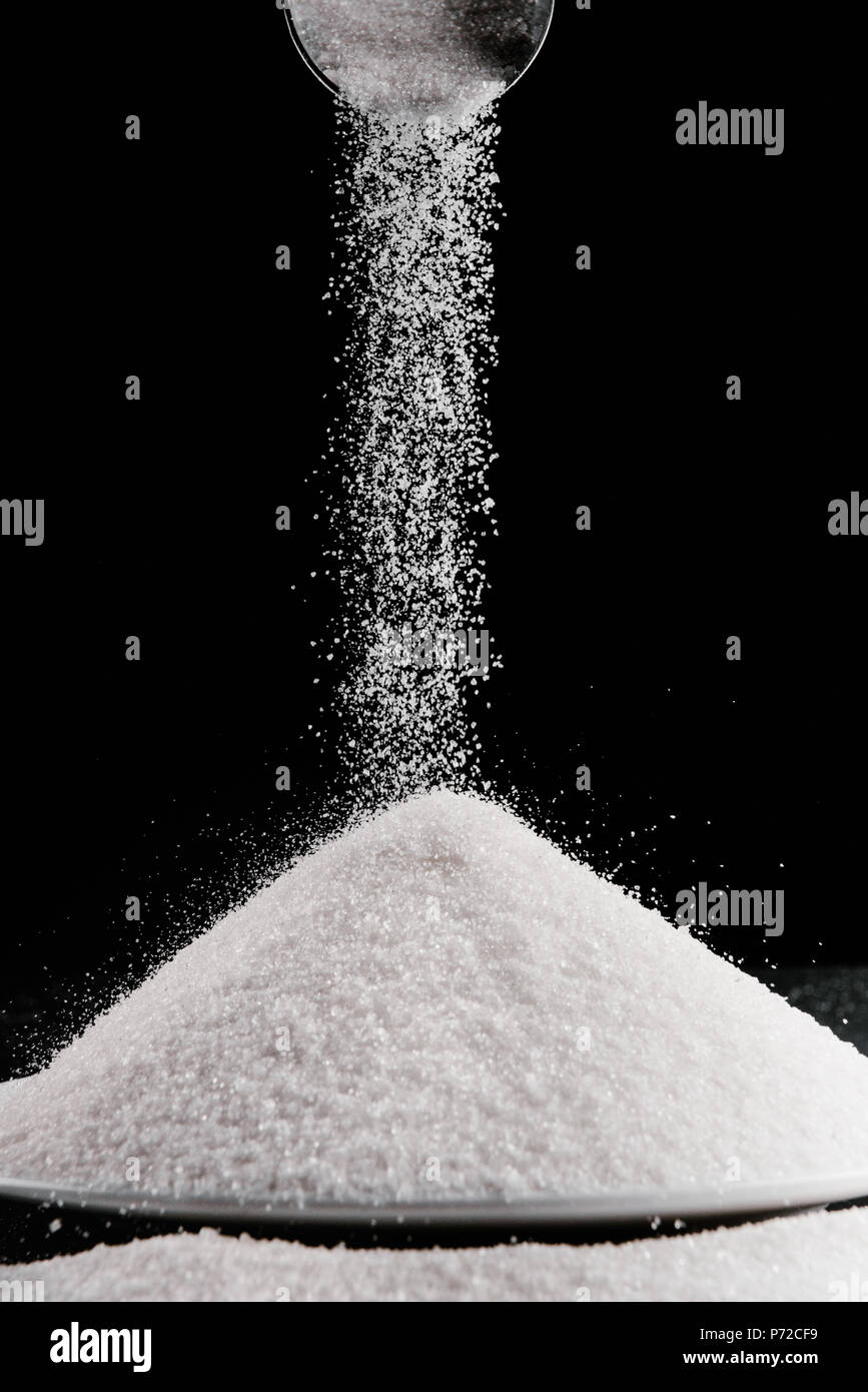 sugar falling from metal scoop on pile on plate isolated on black Stock ...