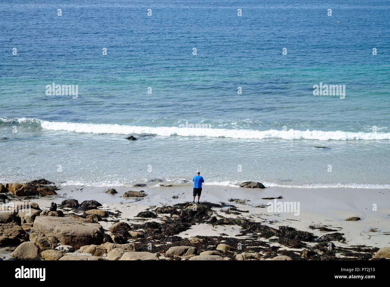 Single male fisherman beach fishing off the beach at Sennen Cove on a ...