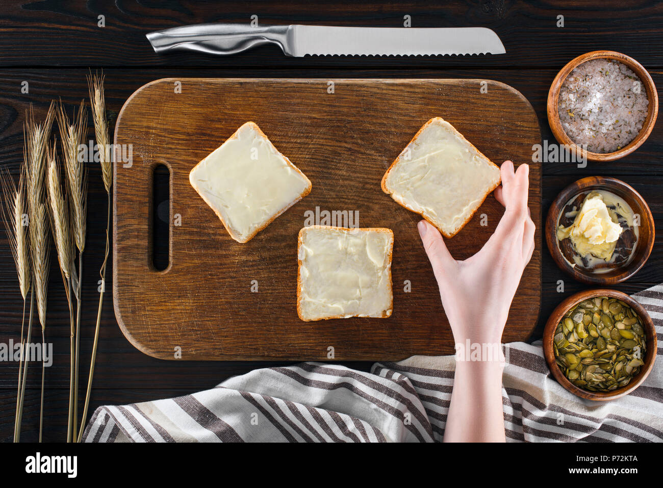 top view of human hand holding fresh toast with butter from wooden ...