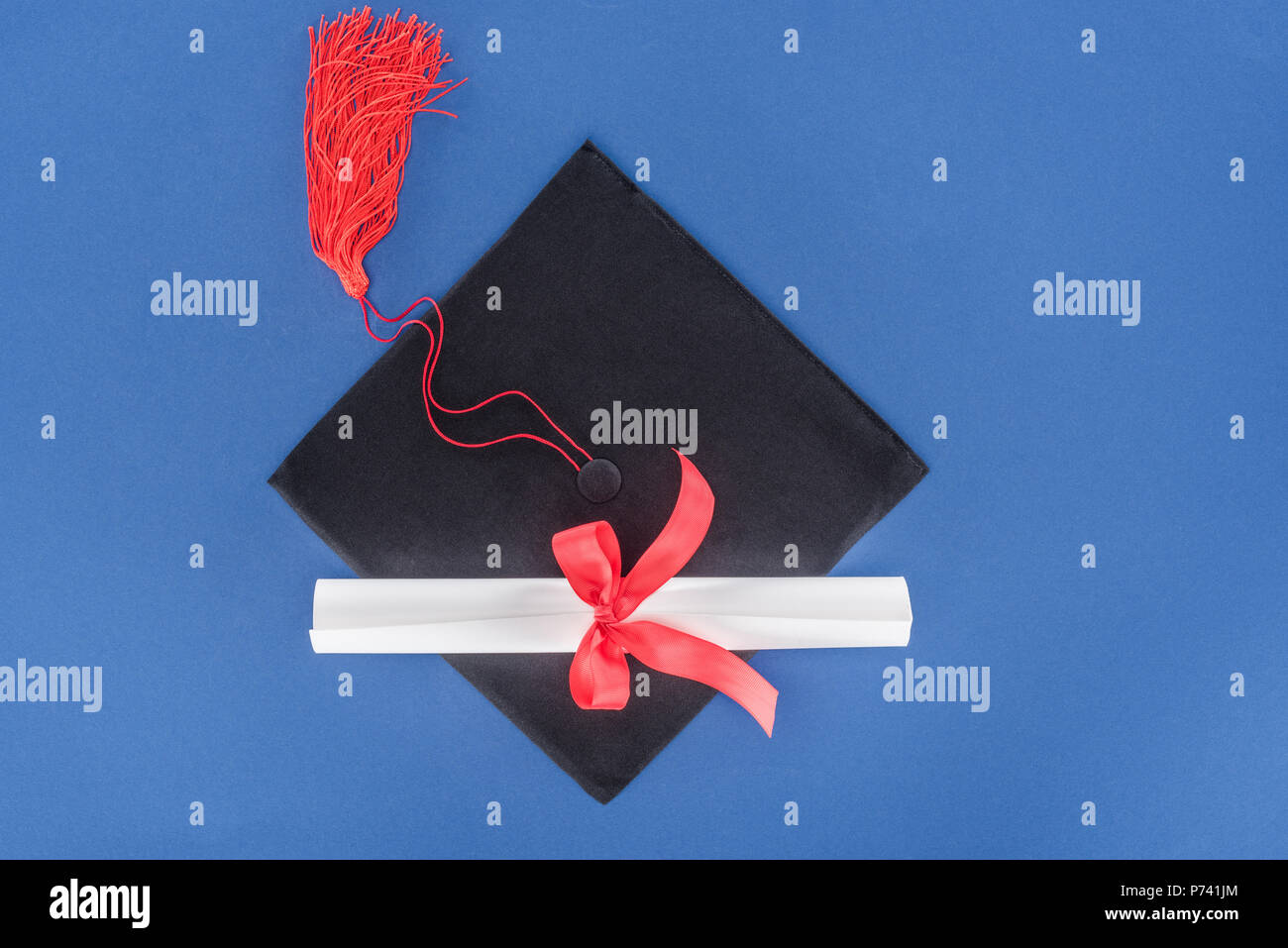 Graduation hat and diploma with red ribbon isolated on blue Stock Photo ...