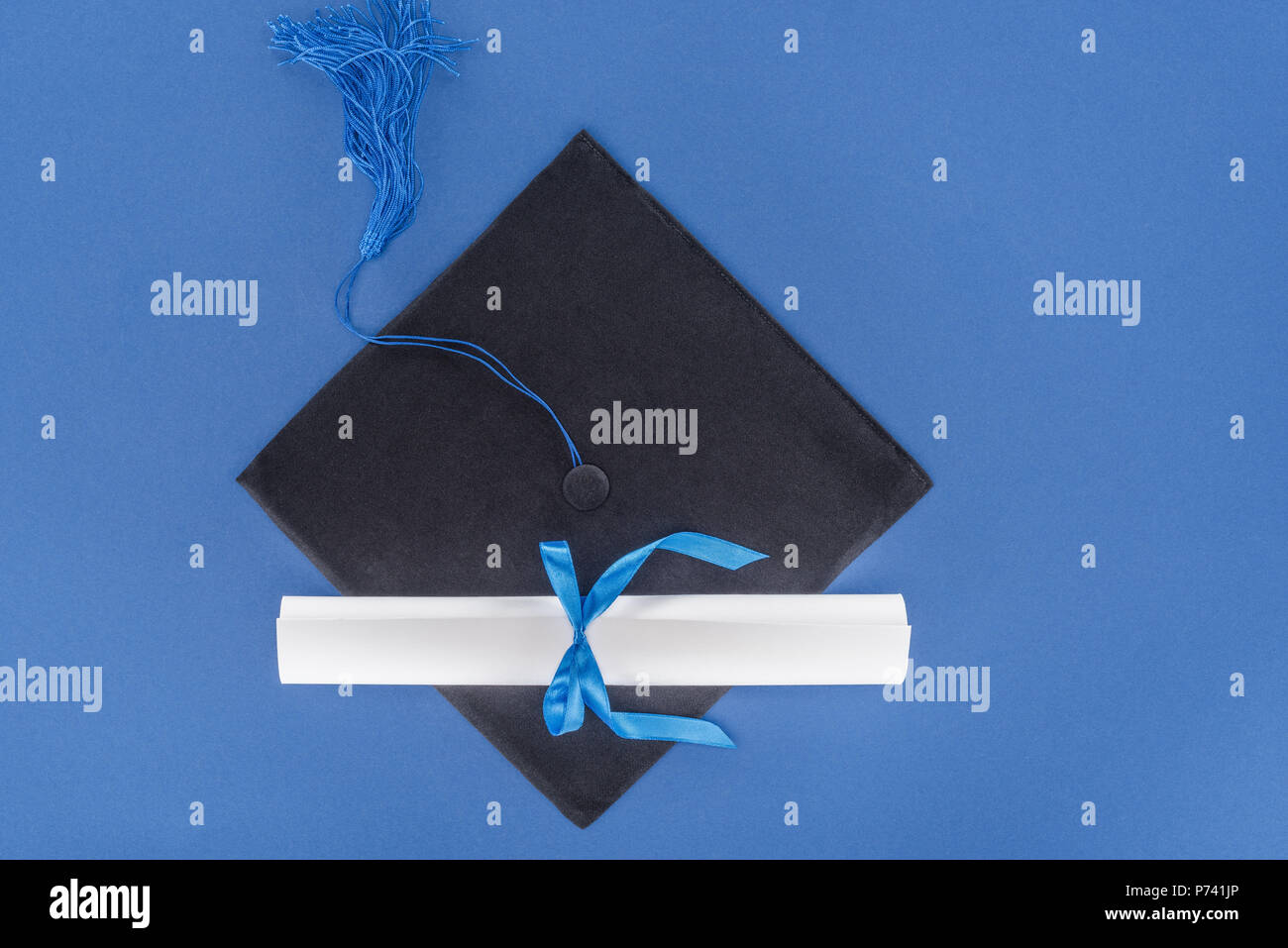 Graduation hat and diploma with blue ribbon isolated on blue Stock ...