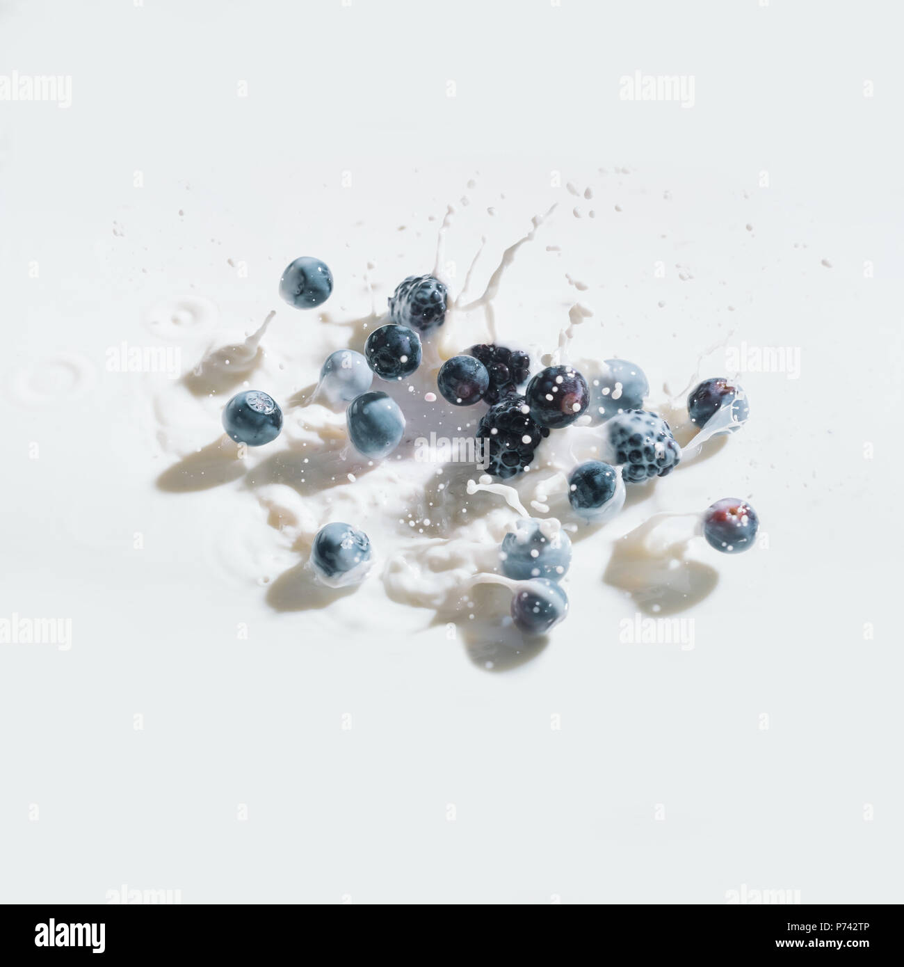 Raw berries dropping in milk with splashes on white background Stock ...