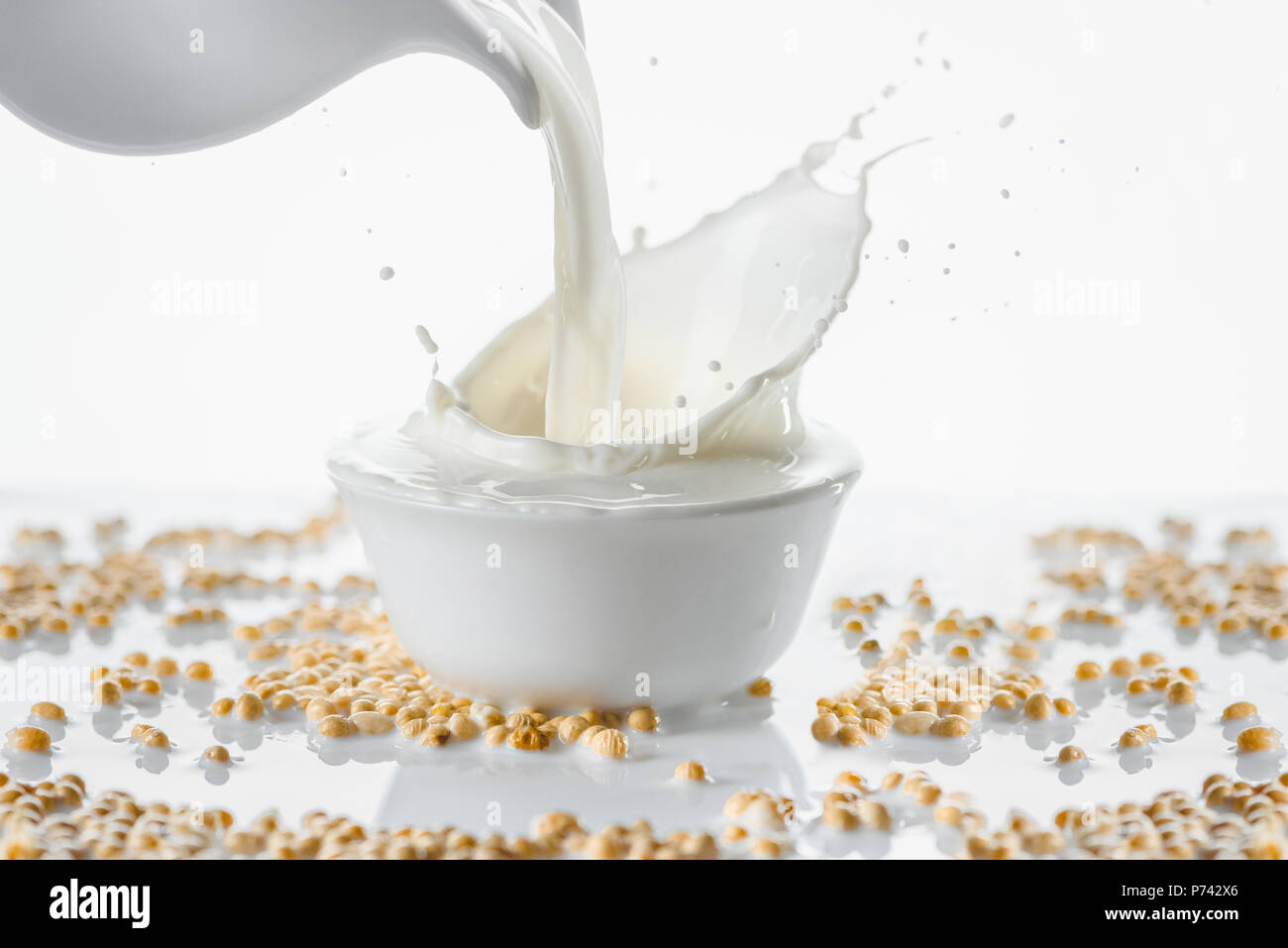 Milk splashing from jug in bowl with soybeans on white background Stock ...