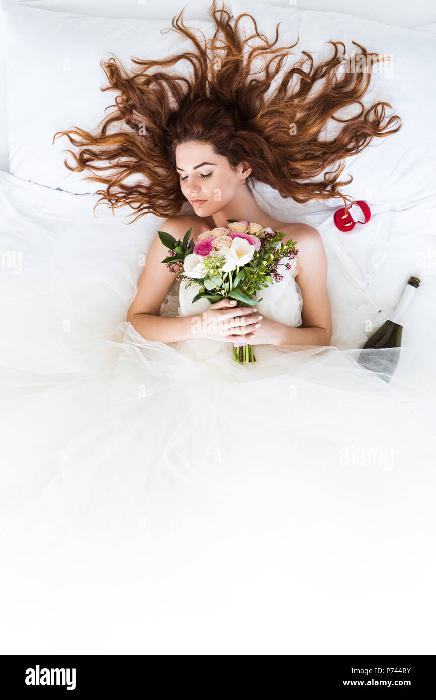 Top view of redhead bride wearing white dress sleeping in bed with ...
