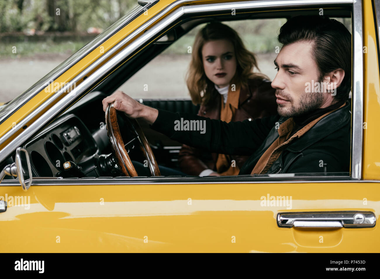 young woman looking at handsome stylish boyfriend driving yellow car ...