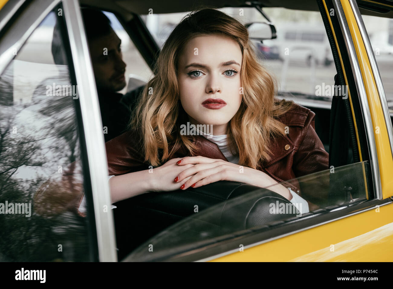 beautiful young woman looking at camera through car window while ...