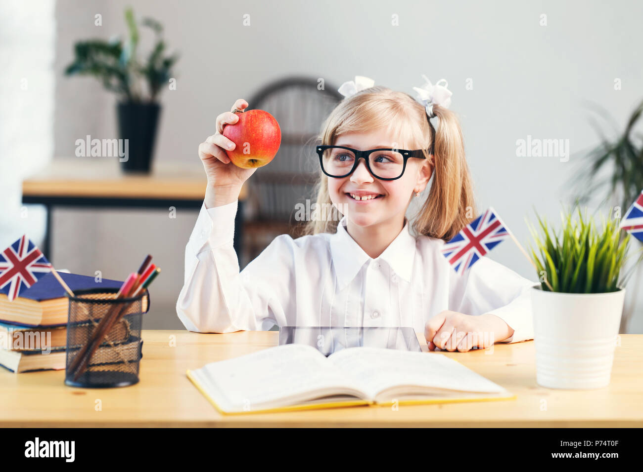 Happy smiling girl learning English language holding red apple in light ...