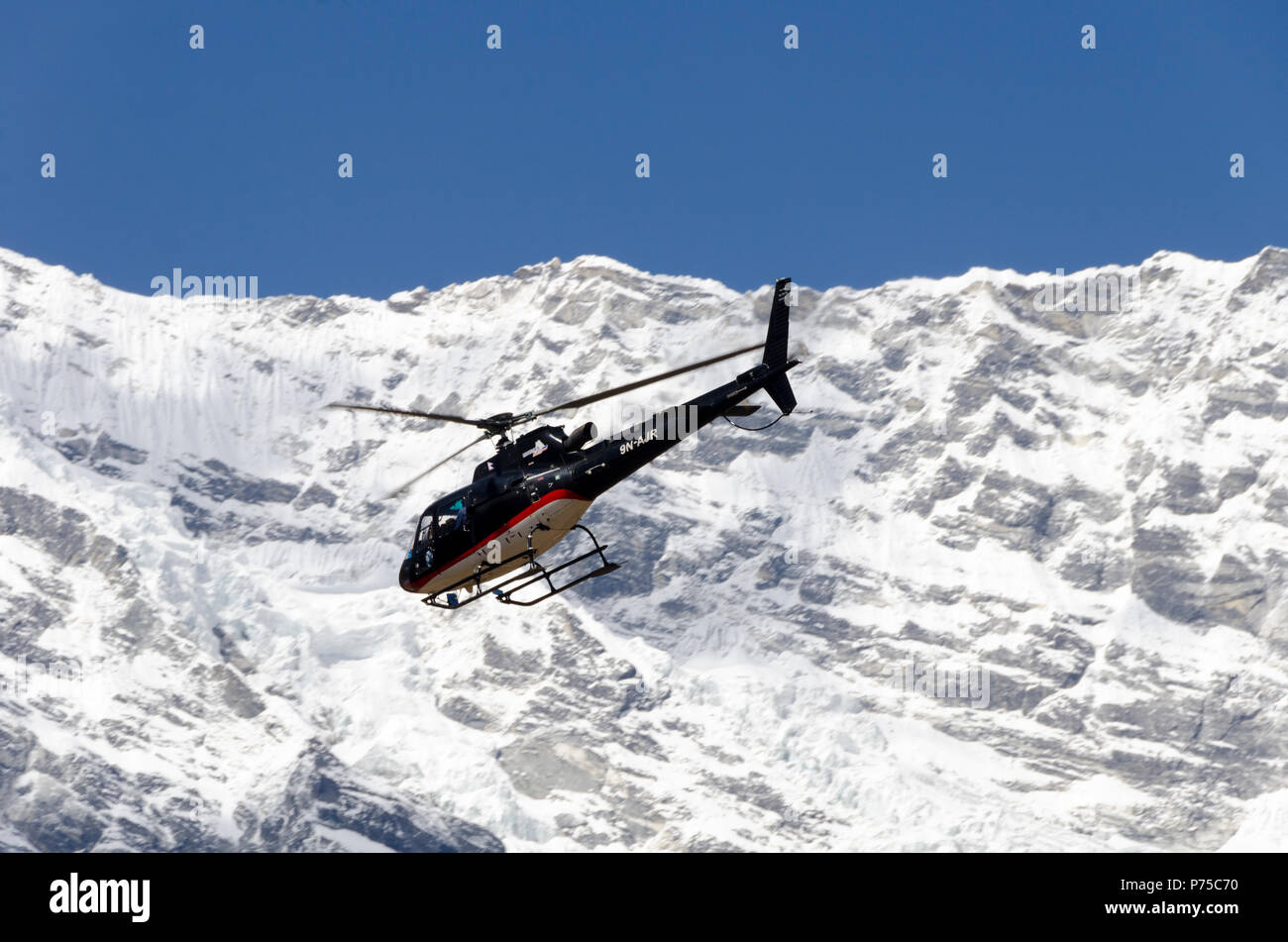 Helicopter flying on front of snow covered mountain face, Kyanjin Gompa ...