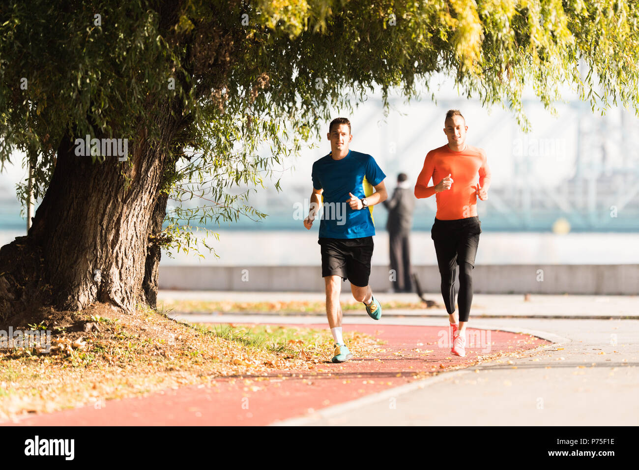 Handsome young men wearing sportswear and running at quay during autumn ...