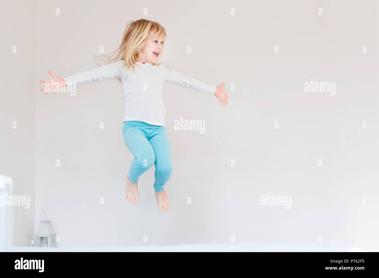 Happy kid jumping over bed. Cute little blond girl having fun indoors ...