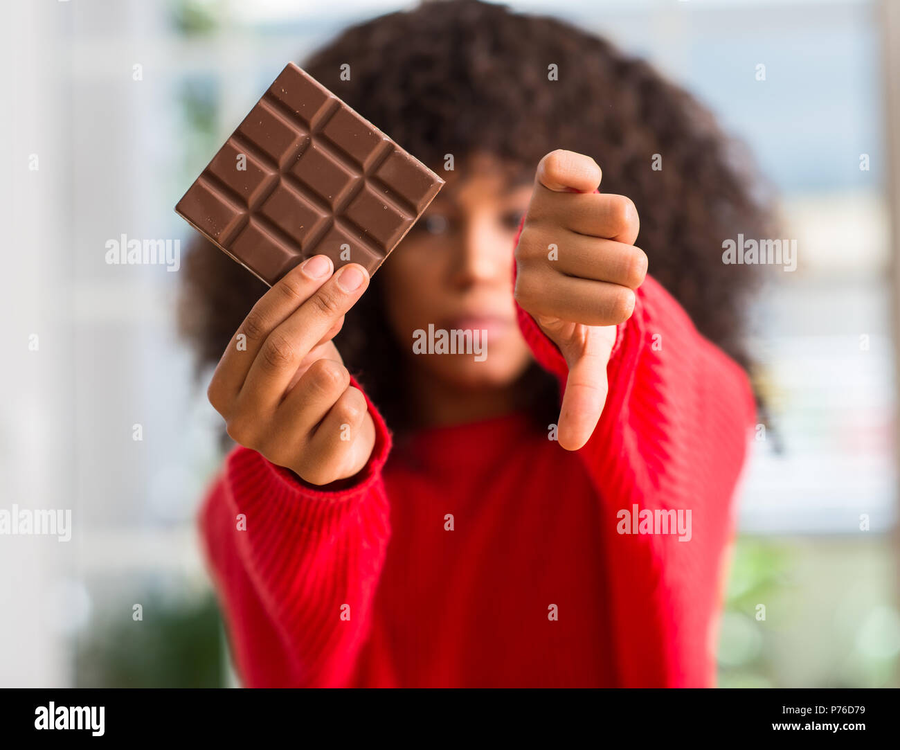 African american woman eating chocolate bar at home with angry face ...
